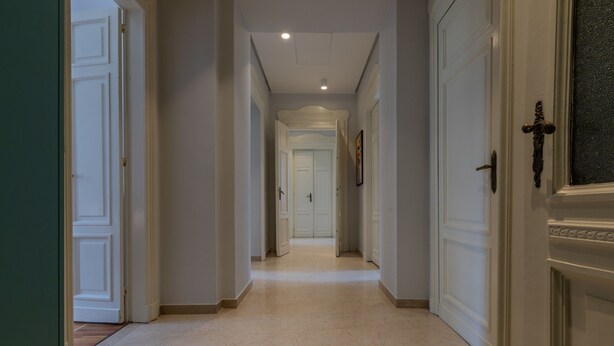 Corredor com portas brancas, piso de mármore e iluminação embutida.