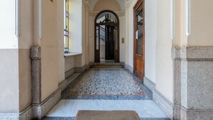 Um corredor com piso ladrilhado, uma porta de madeira no final e um luminário acima.