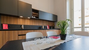 Cozinha moderna com armários escuros, parede de destaque em madeira e área de jantar com mesa posta para dois.