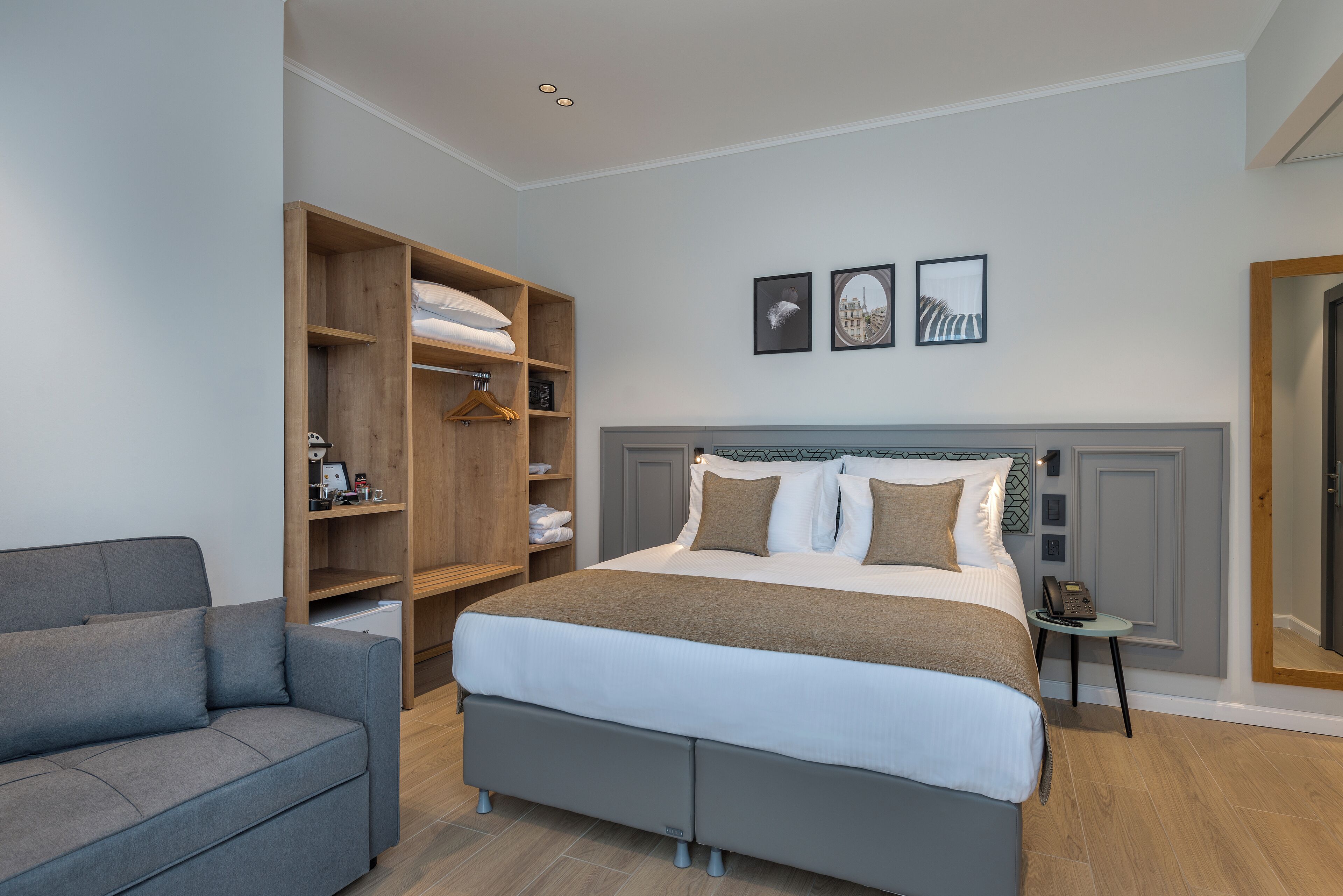 Quarto moderno com uma cama grande, um sofá cinzento, um guarda-roupa de madeira e uma pequena mesa de cabeceira com um telefone.
