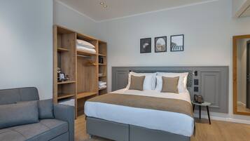 Quarto moderno com uma cama grande, um sofá cinzento, um guarda-roupa de madeira e uma pequena mesa de cabeceira com um telefone.