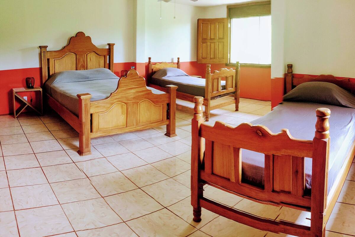 Quarto com duas camas de madeira, uma mesinha e um ventilador de teto.
