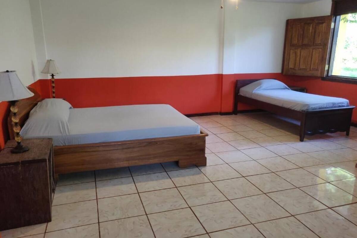 Quarto com duas camas de madeira, um ventilador de teto e uma janela com vista.