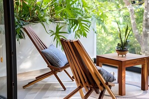 Uma cadeira de madeira com almofada, uma pequena mesa de madeira e um vaso com planta.