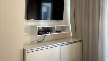 Quarto de hotel com televisão de tela plana na parede, um minibar branco e uma cama com edredom branco.