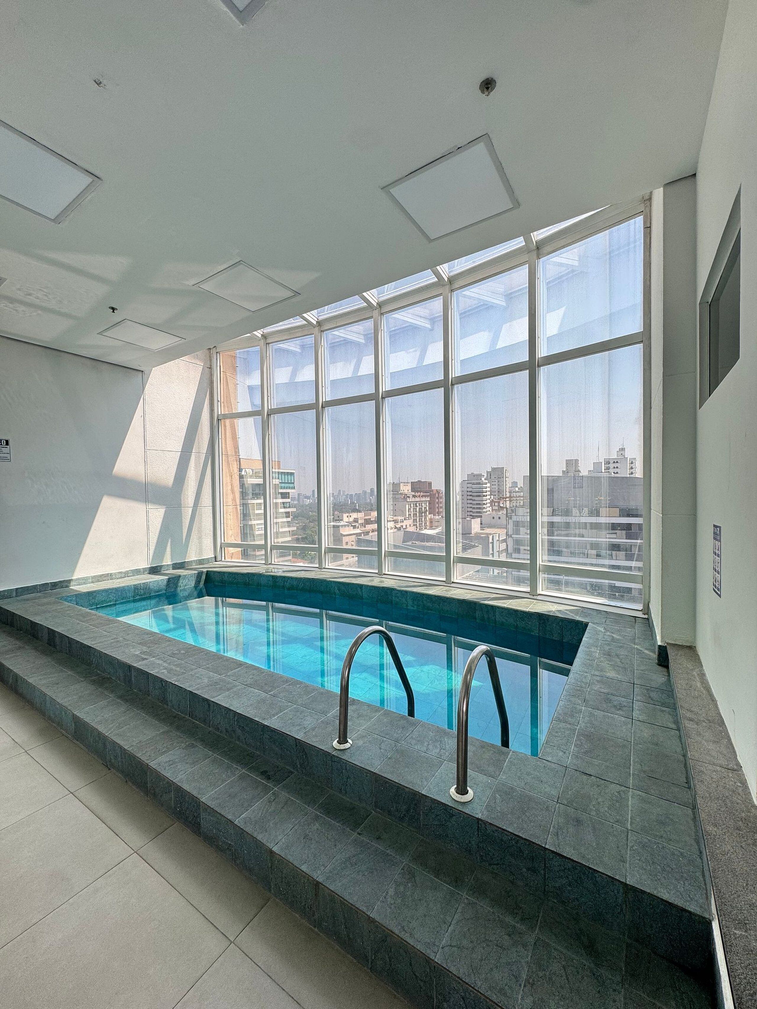 Piscina interior moderna com vista para a cidade através de grandes janelas.
