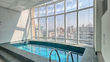 Piscina interior moderna com vista para a cidade através de grandes janelas.