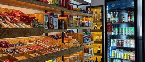 Uma área de lanches e bebidas, com prateleiras cheias de diversos petiscos e um refrigerador com bebidas.