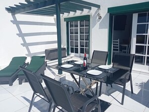 Um pátio com uma mesa posta para dois, duas cadeiras e uma estrutura de pérgola.