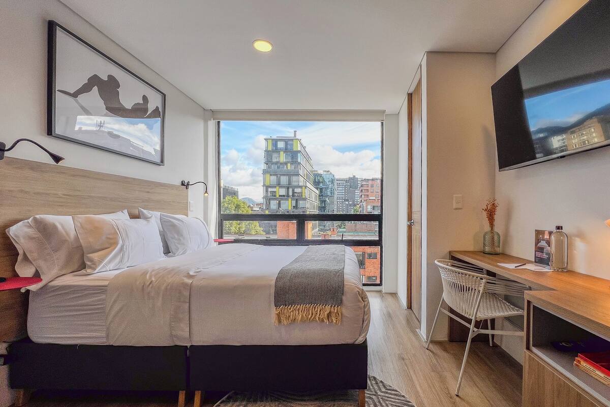 Quarto de hotel moderno com uma cama grande, uma escrivaninha e uma televisão.