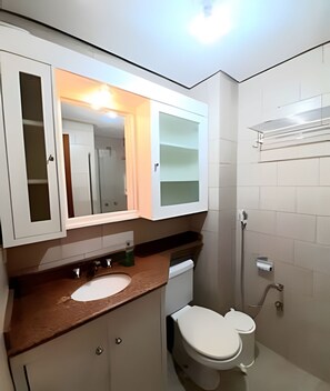 Casa de banho compacta com lavatório branco, sanita e armário com porta de vidro sobre o lavatório.