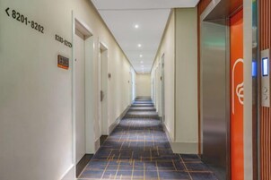 Corredor de hotel com placas de sinalização, um elevador e um tapete estampado.