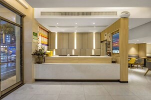 Uma área de recepção de hotel com balcão, assentos e vista para a rua.