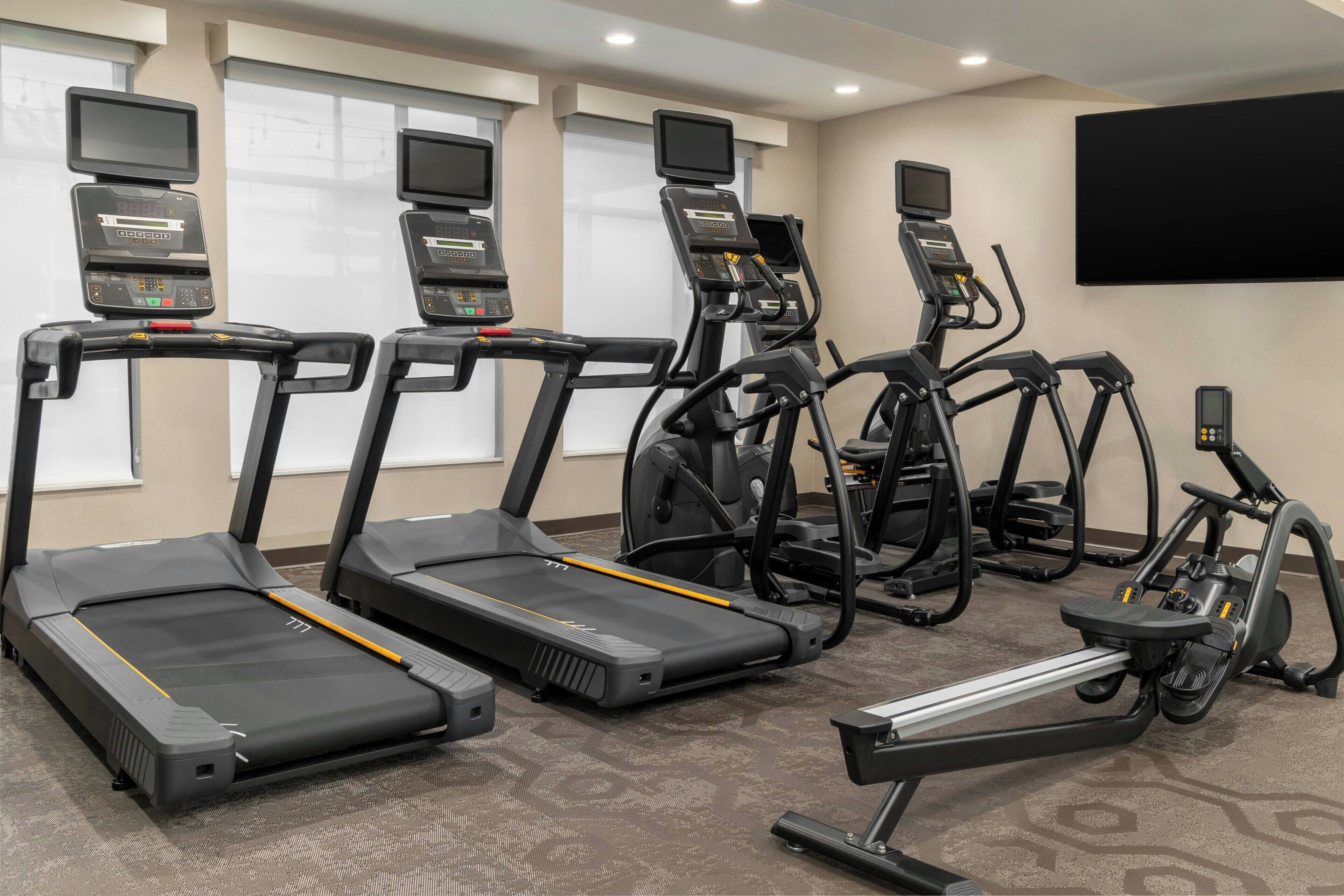Uma sala de ginástica com esteiras, elípticos e bicicleta ergométrica.