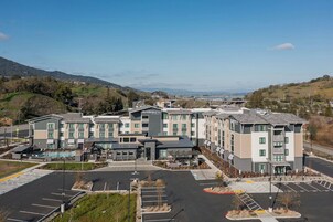 Um hotel com vários andares e design moderno, com um pátio central, estacionamento e vista para a paisagem circundante.