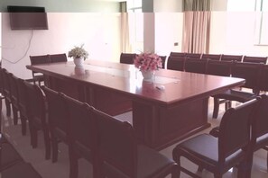 Uma sala de conferências com uma mesa comprida, cadeiras e uma televisão fixada na parede.