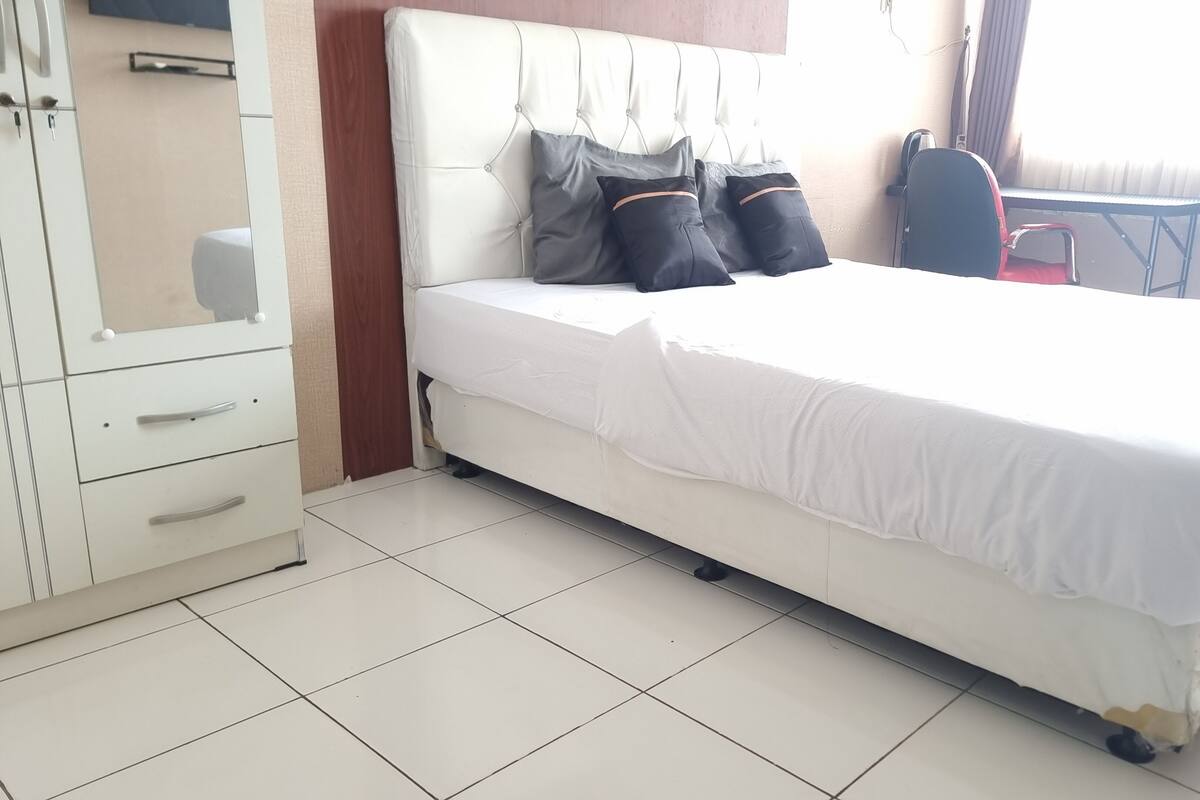 Quarto de hotel com cama branca, guarda-roupa e uma cadeira.