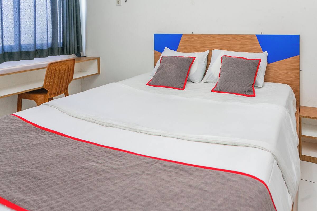 Cama bem arrumada com manta branca e cinza, duas almofadas e cabeceira de madeira com detalhe azul.