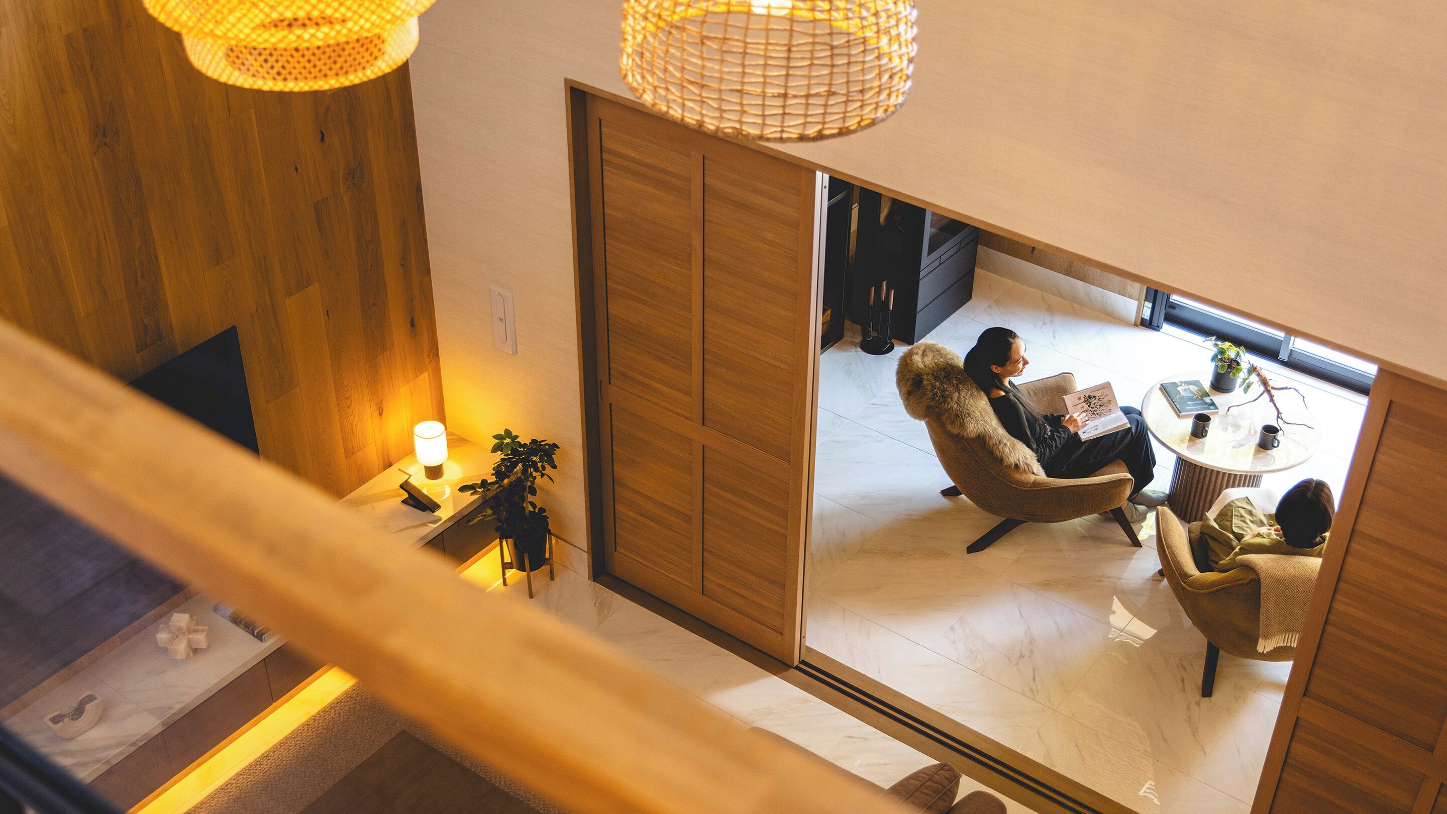 Interior moderno com piso de madeira, um espelho grande refletindo um ambiente com sofá, mesa e planta em vaso.