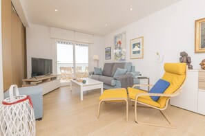 Sala moderna com sofá, poltrona amarela, TV e varanda com vista.