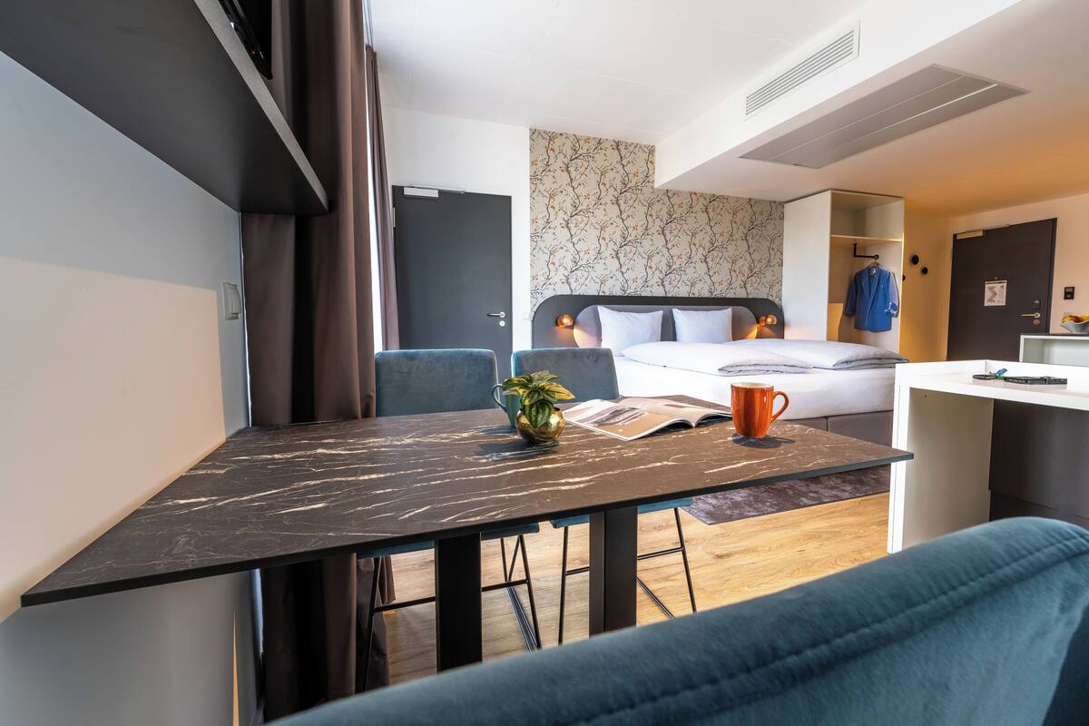 Quarto de hotel moderno com cama, escrivaninha, cadeira e mesa de jantar.