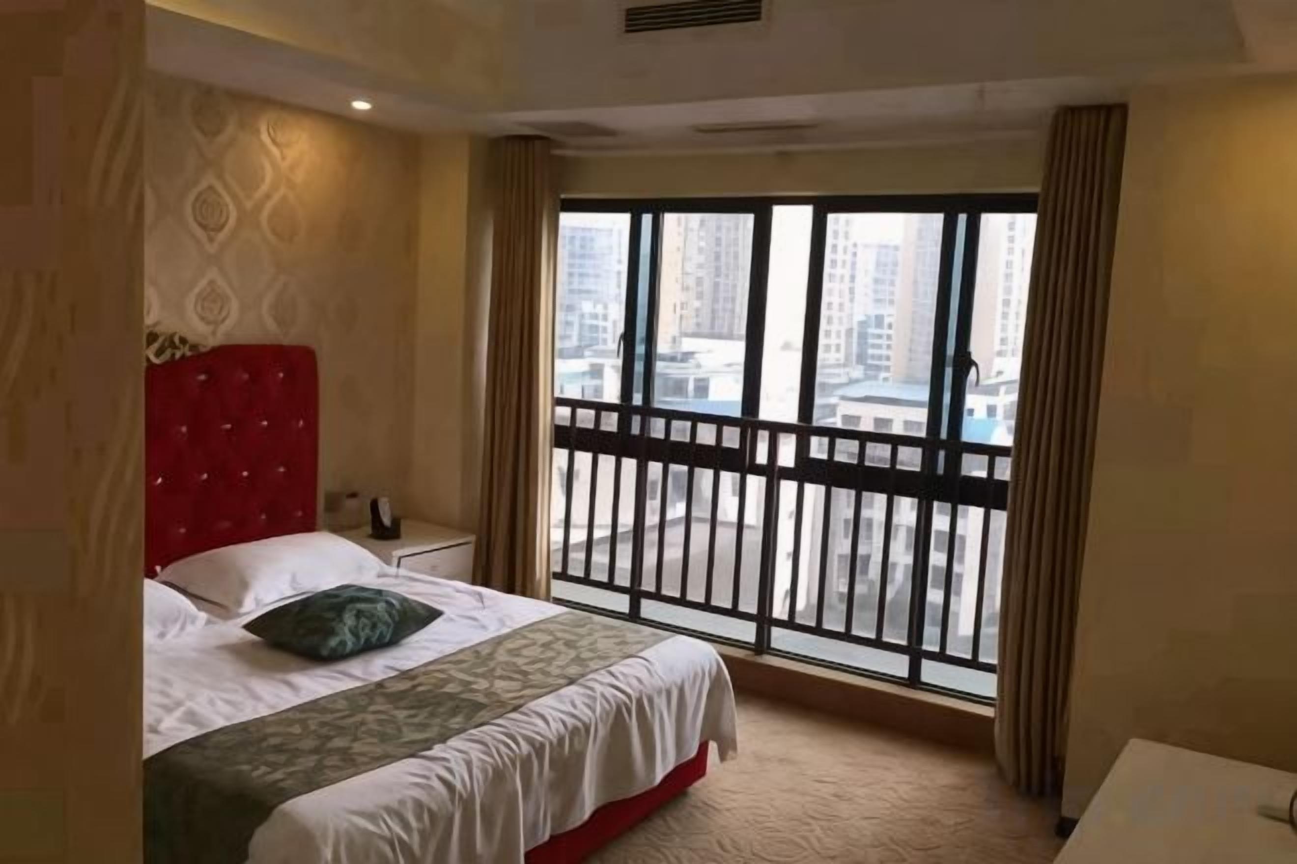 Quarto de hotel com uma cama grande, uma mesa de cabeceira e uma janela com vista para edifícios.