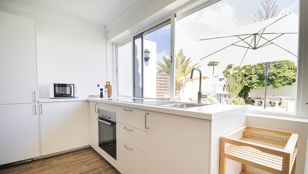 Uma cozinha moderna com armários brancos, forno embutido e janela com vista para um jardim.