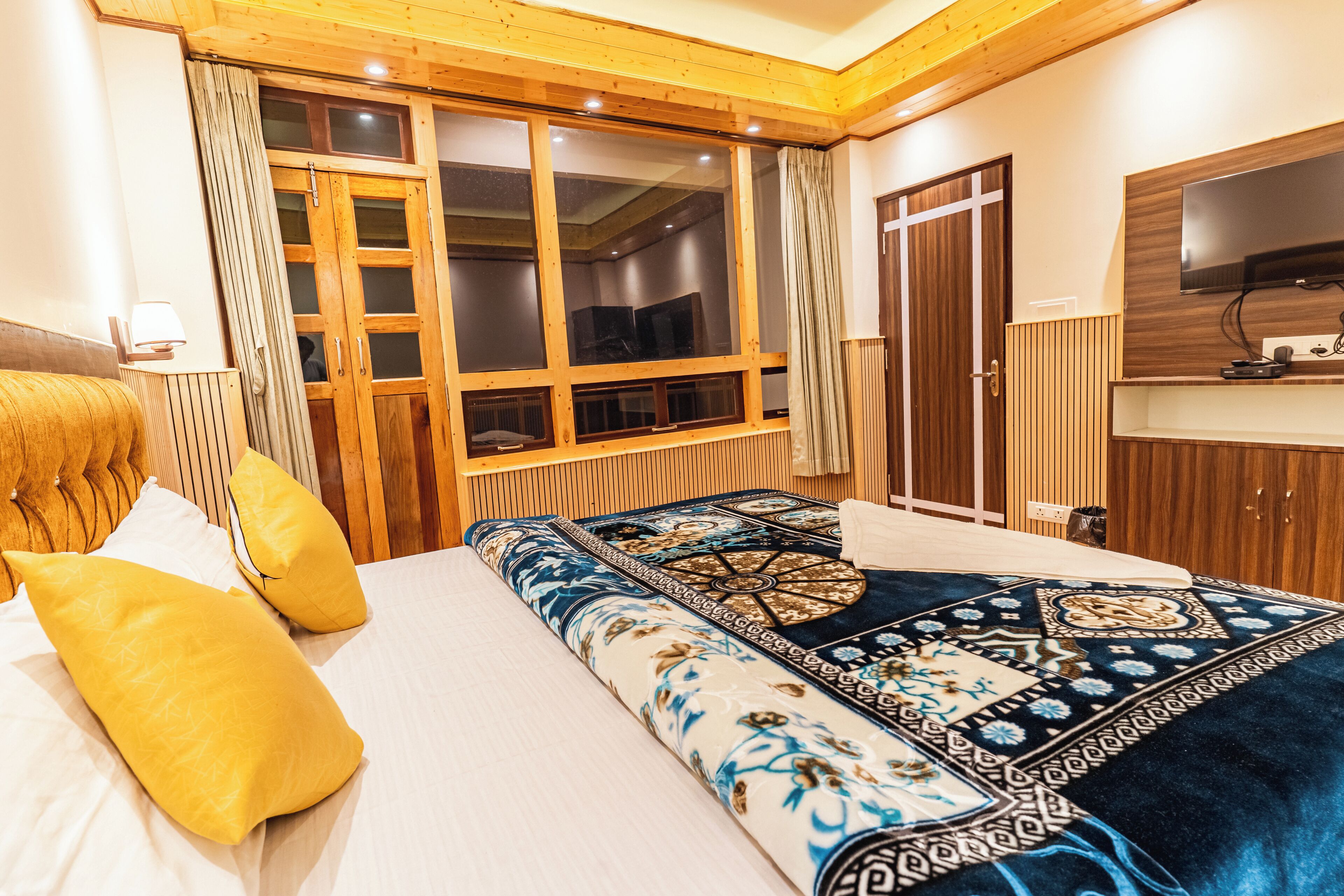 Quarto com cama, janela grande, televisão e painéis de madeira.
