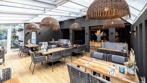 Restaurante moderno com pé direito alto, janelas amplas e luminárias pendentes de vime.