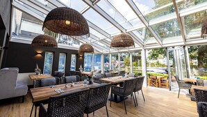 Um restaurante moderno com paredes de vidro, mobiliário de vime e iluminação natural.