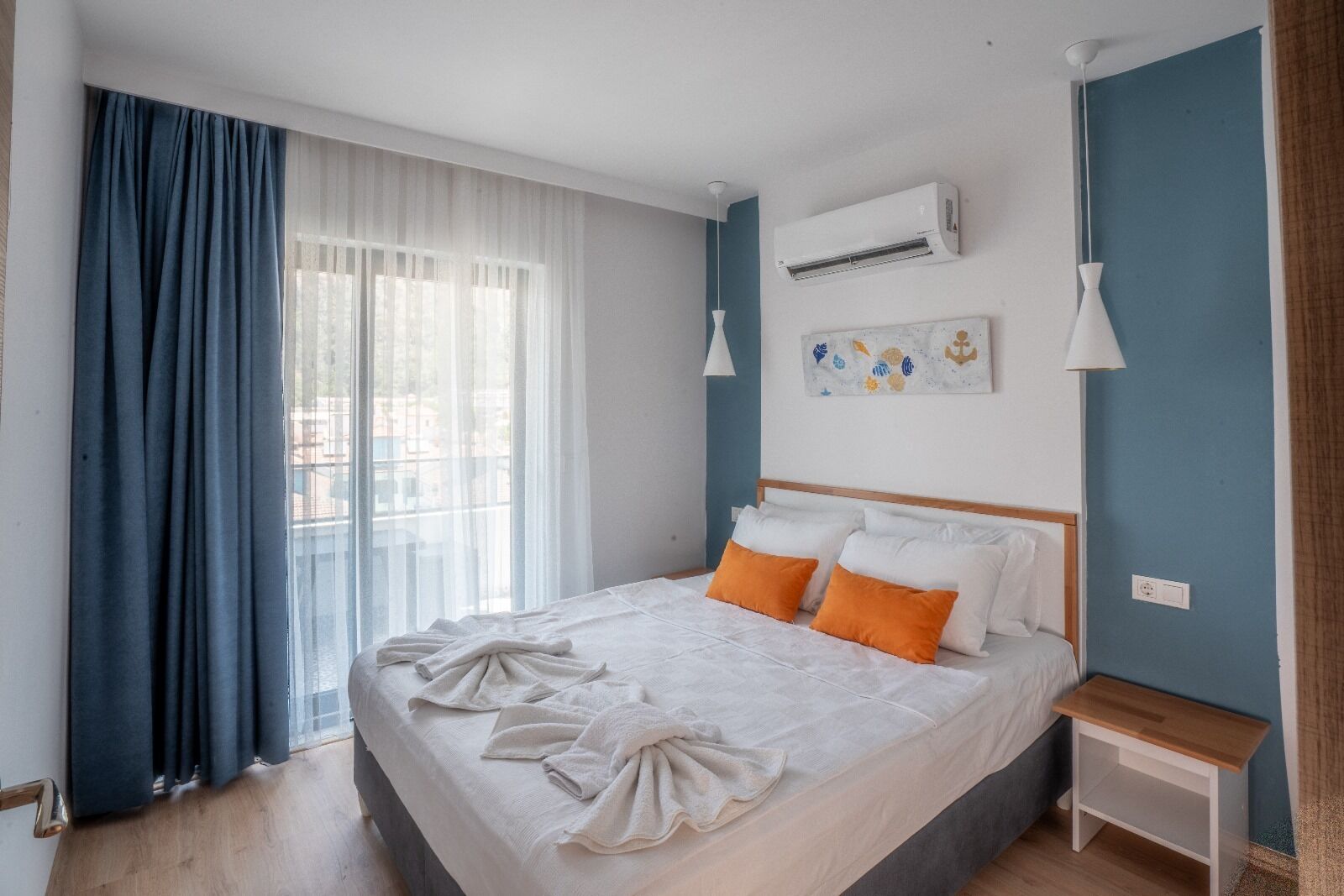 Quarto de hotel com uma cama, mesa de cabeceira, aparelho de ar condicionado e janela com cortinas.