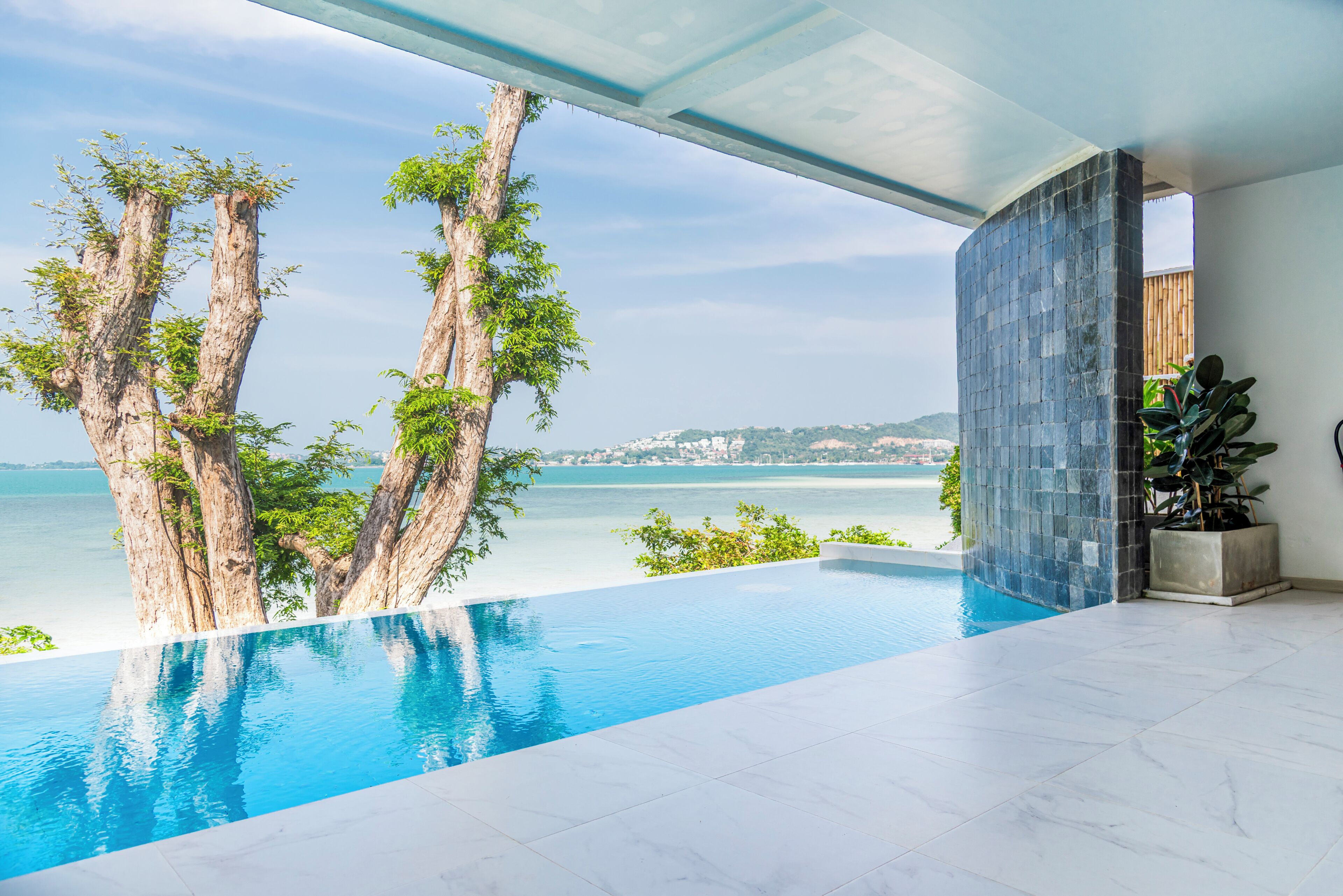 Uma piscina infinita moderna com vista desimpedida para o mar e paisagem urbana ao fundo.