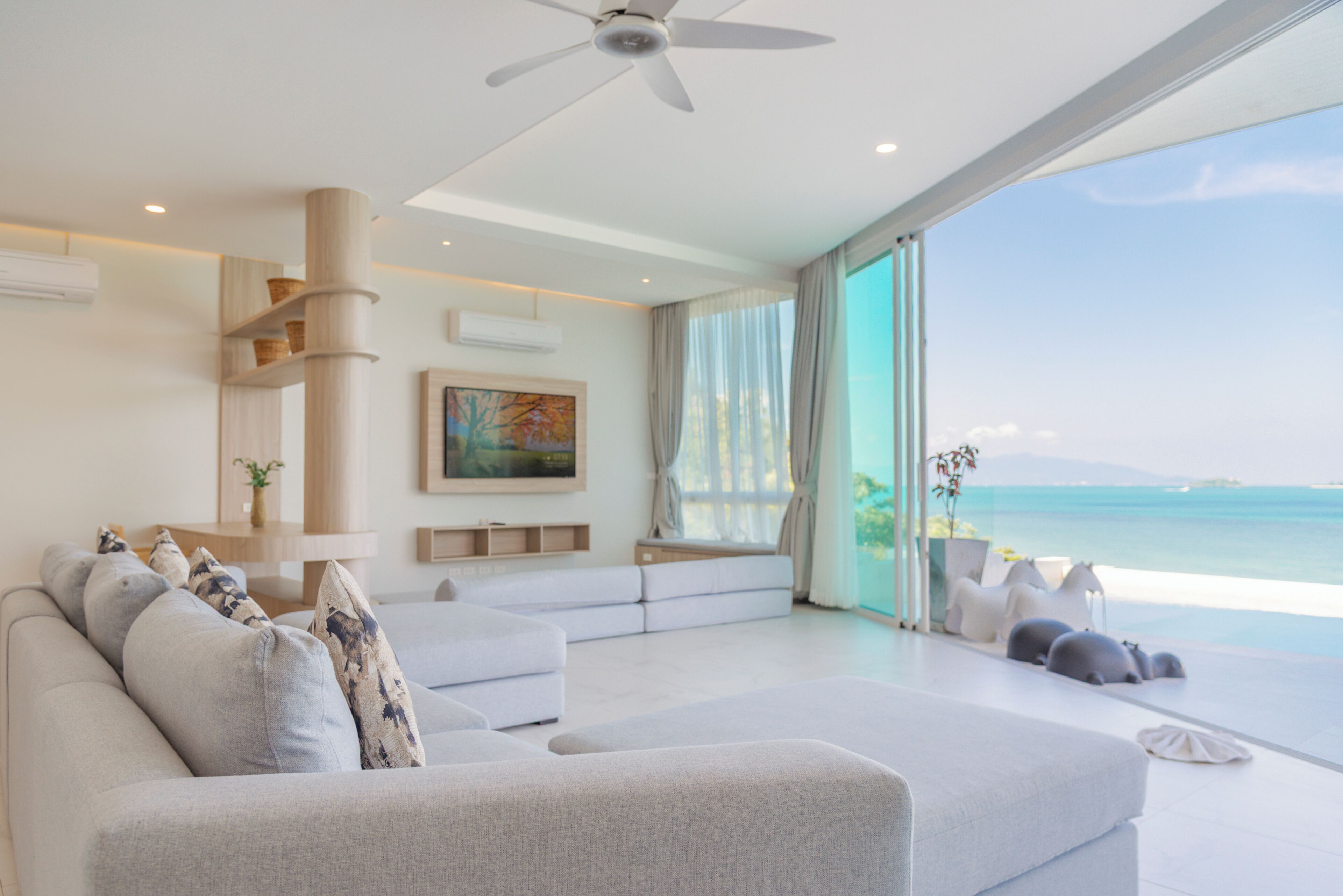Uma sala de estar moderna com um sofá grande, um quadro e vista para o mar.