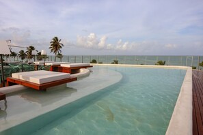 Área de piscina com espreguiçadeiras e vista para o mar.