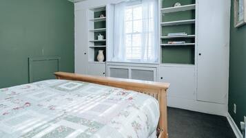 Quarto com cama, janela com cortinas, estante embutida e radiador.