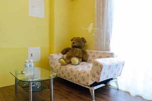 Um quarto com uma mesa de vidro, um sofá floral e um urso de pelúcia grande.