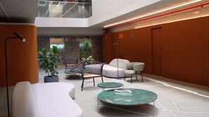 Um hall moderno com um sofá branco curvo, uma cadeira de metal, uma mesa de mármore verde e painéis de madeira nas paredes.