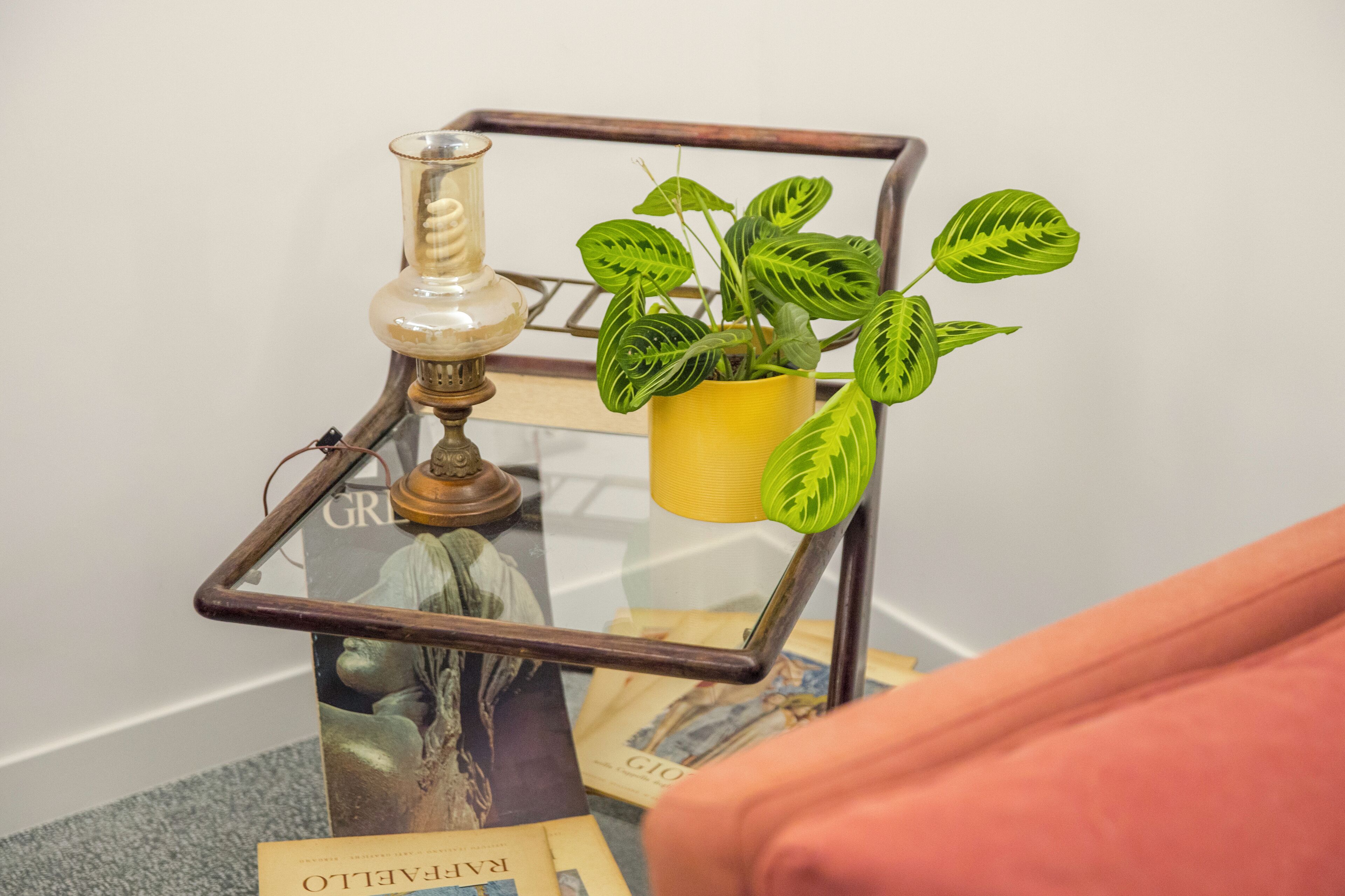 Uma mesinha lateral com tampo de vidro, uma luminária de latão, um vaso com planta e um livro intitulado "GIO".