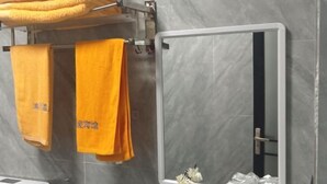 Uma casa de banho com um porta-toalhas com dois toalhas, um espelho e uma pia com artigos de higiene pessoal.