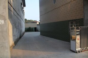 Uma passagem estreita com piso de concreto, um portão de metal e um edifício de tijolos com uma persiana metálica.