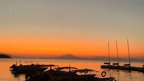Um pôr do sol sobre uma marina, com barcos atracados e a superfície da água calma.