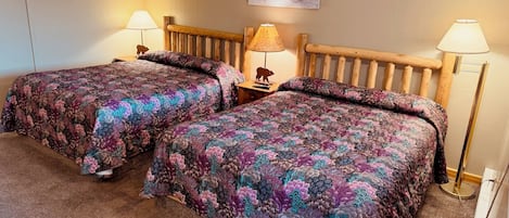 Quarto com duas camas, cada uma com colcha estampada e cabeceira de madeira, além de duas luminárias de cabeceira.