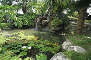 Um jardim tranquilo com lago, vegetação exuberante e uma pequena cascata.