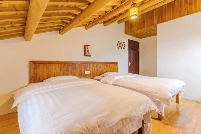 Quarto com duas camas, vigas de madeira no teto, cabeceira de madeira, uma porta e um ponto de luz.