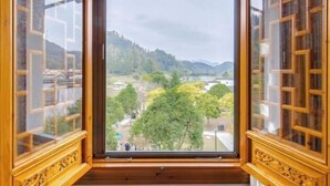 Quarto com uma janela grande que oferece vista para uma paisagem verde com árvores e colinas.