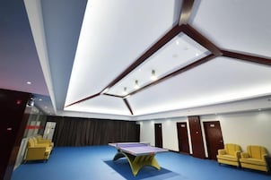 Quarto com mesa de pingue-pongue, carpete azul e design moderno no teto.