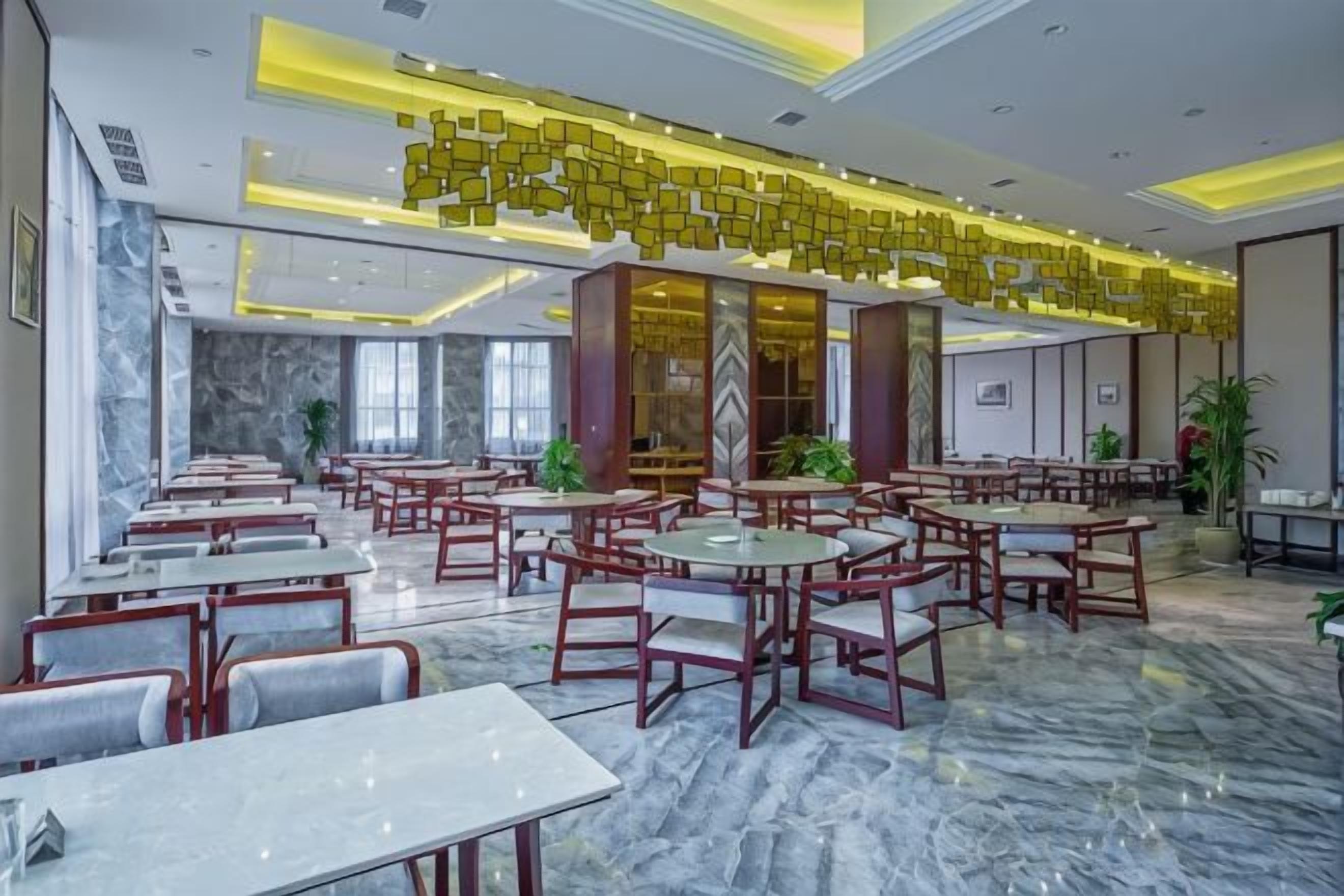 Uma sala de jantar ampla com várias mesas e cadeiras, piso de mármore e design de teto moderno.