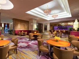 Um saguão de hotel com mesas redondas, assentos confortáveis, balcão de recepção e área de bar.