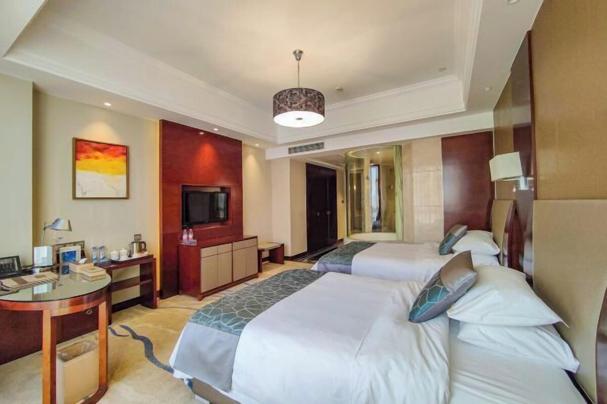 Quarto de hotel com duas camas, uma escrivaninha, televisão, espelho e um quadro na parede.