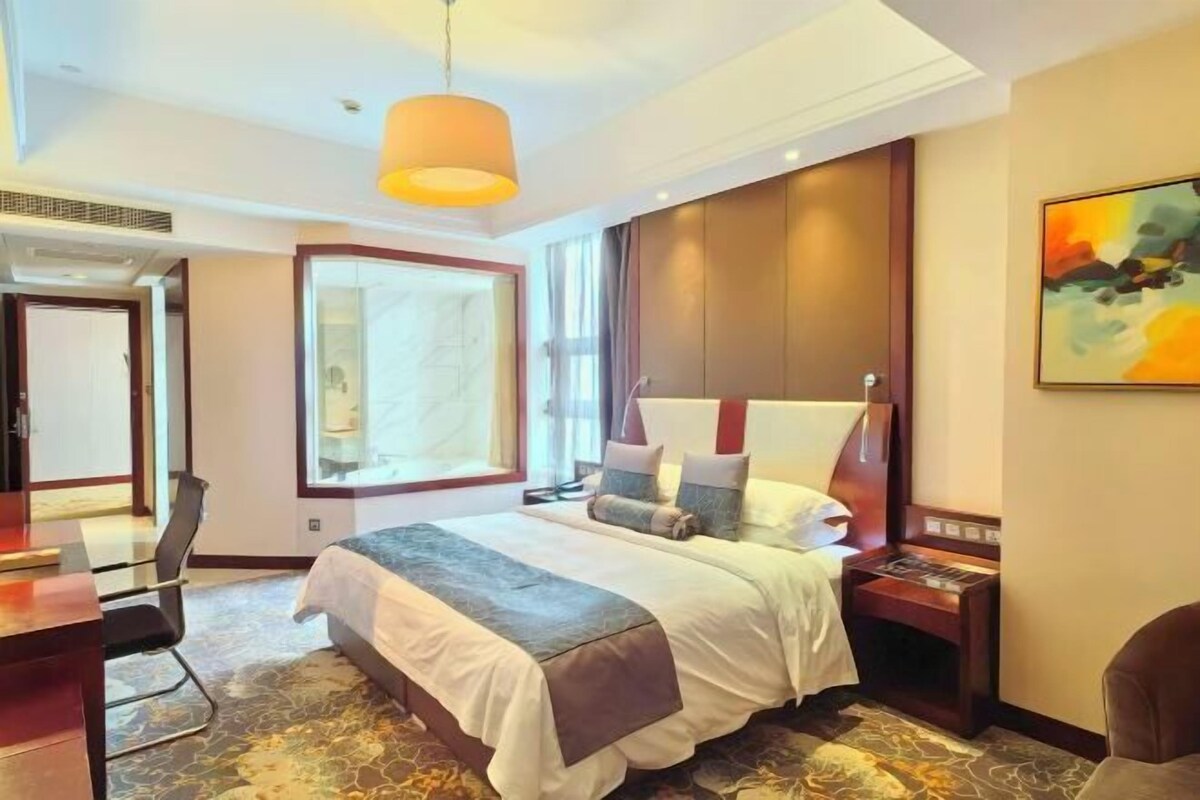 Quarto de hotel com uma cama grande, uma escrivaninha, uma cadeira e uma janela.